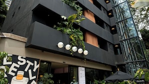 Um edifício moderno com vários andares, área externa com mesas e cadeiras e plantas em vasos, e uma placa indicando uma cafeteria.