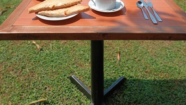 Uma mesa de madeira com itens de café da manhã, incluindo doces, frutas e um copo de suco de laranja, montada ao ar livre perto de uma piscina.
