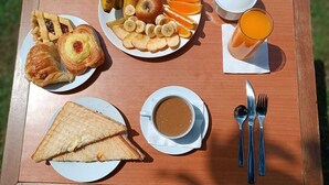 Uma mesa de madeira com uma toalha de piquenique, comida e bebida, incluindo sanduíches, frutas e uma xícara de café.