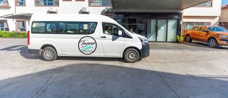 Uma carrinha branca estacionada em frente a um edifício com entrada moderna e várias janelas.