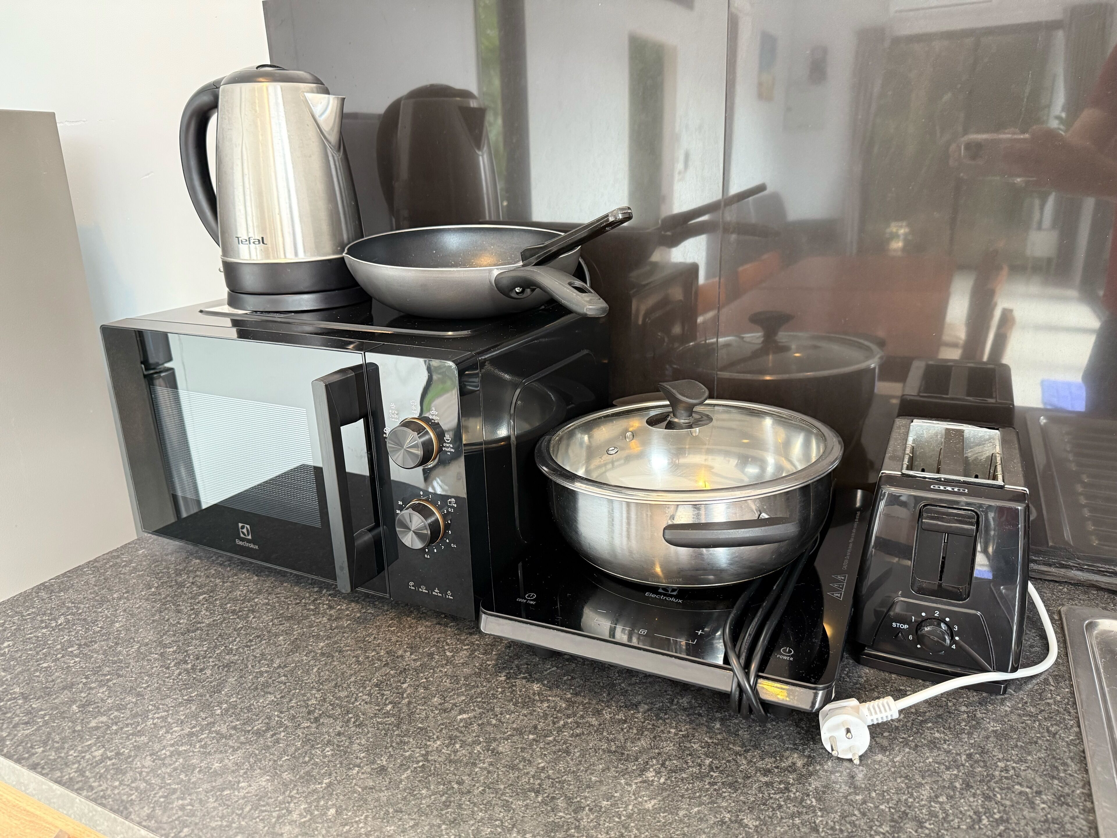 Uma cozinha compacta com fogão, chaleira, frigideira e panela sobre o balcão.