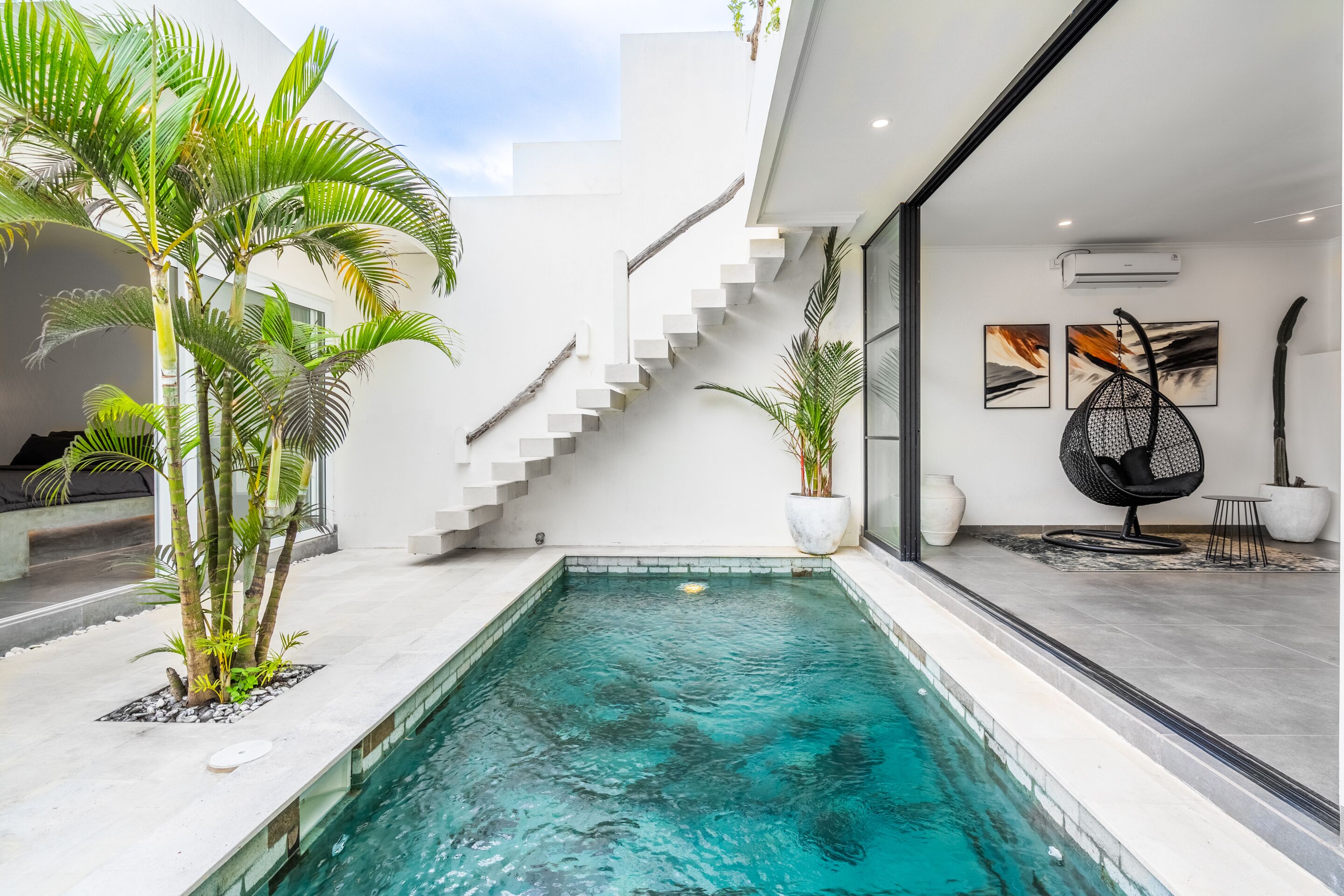 Uma área de piscina moderna ao ar livre, com escadaria, plantas em vasos e móveis minimalistas.
