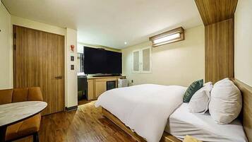 Quarto de hotel com uma cama, uma mesinha, cozinha compacta e televisão.