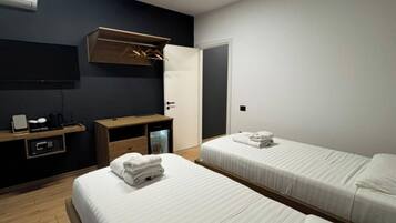 Quarto de hotel moderno com duas camas de solteiro, escrivaninha de madeira, televisão de tela plana e aquecedor embutido.