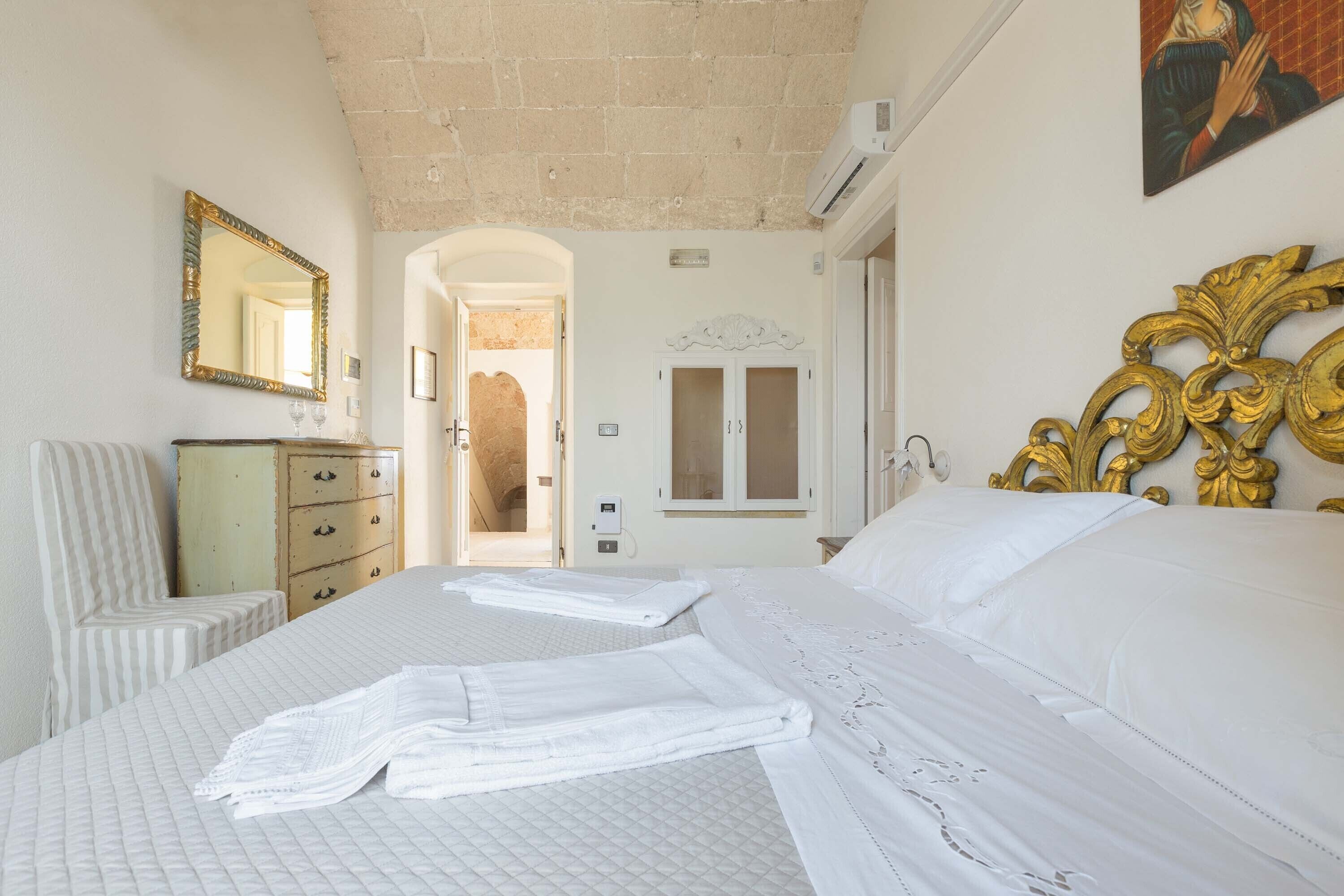 Quarto de hotel com uma cama grande, penteadeira, espelho e porta que dá para outro aposento.