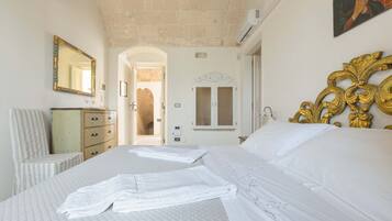 Quarto de hotel com uma cama grande, penteadeira, espelho e porta que dá para outro aposento.