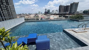 Piscina no terraço com cadeiras azuis e vista desobstruída da paisagem urbana.