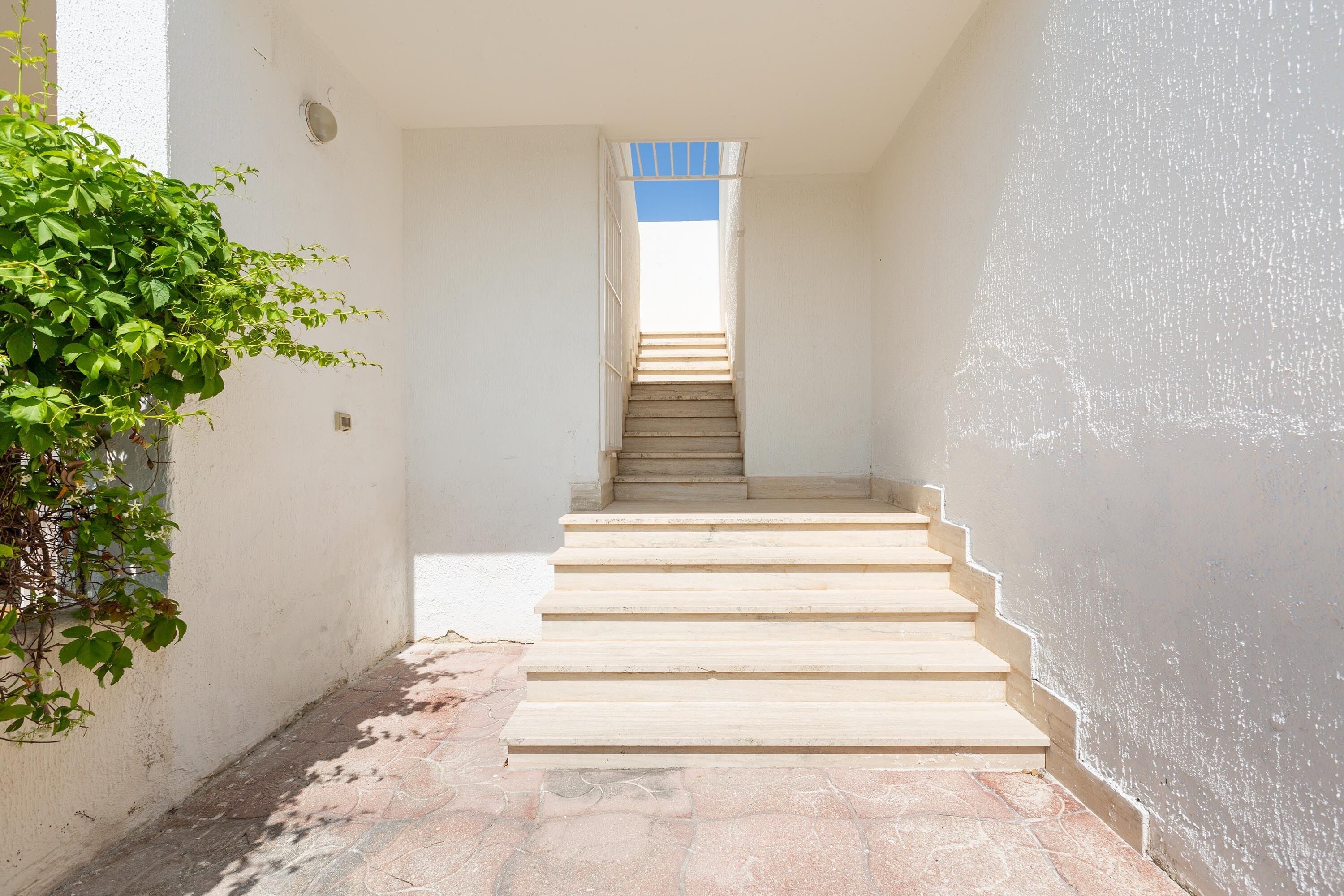 Uma escadaria estreita, com azulejos, leva a um quarto claro com janela.