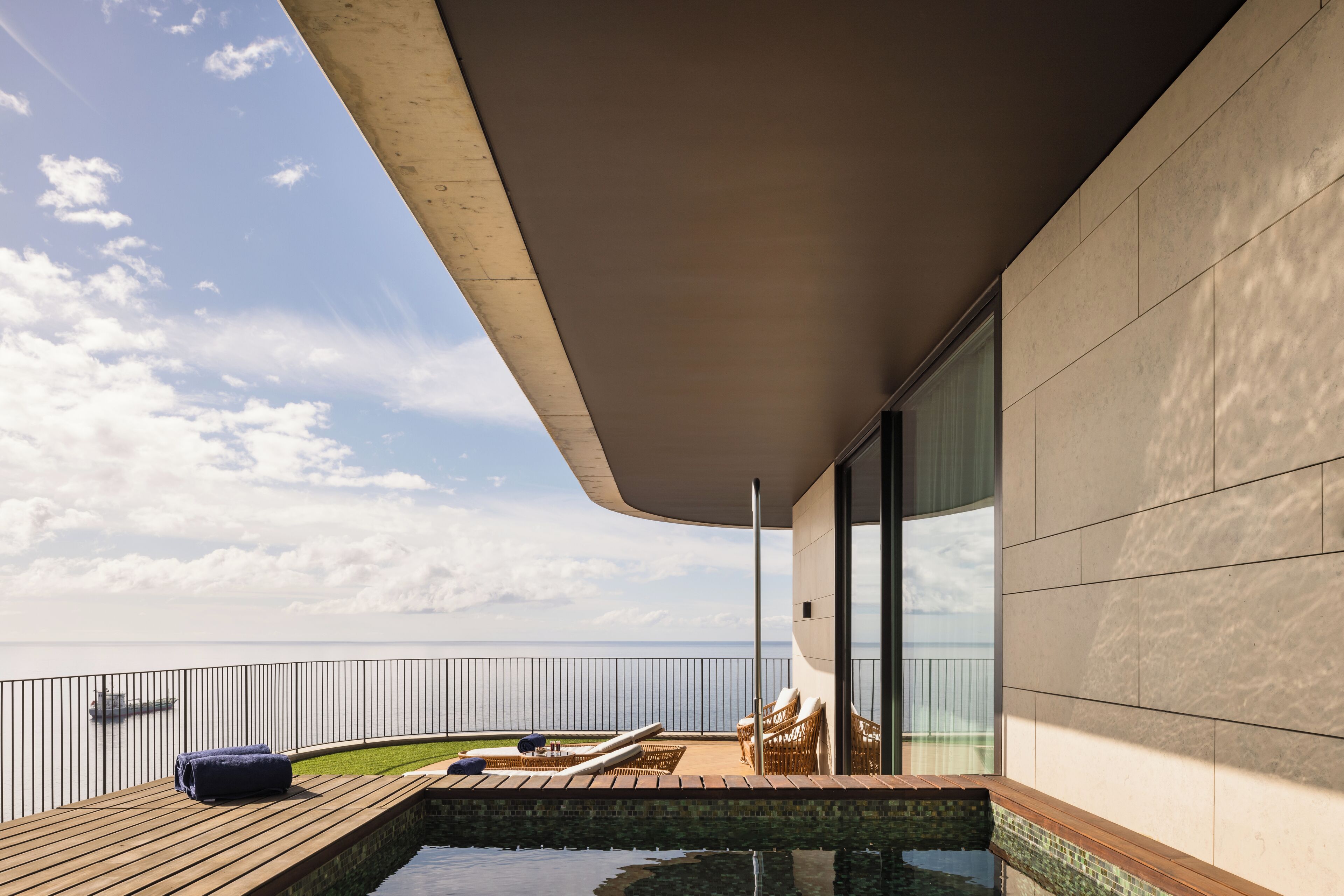 Uma varanda moderna com piscina, espreguiçadeiras e vista para o mar.
