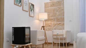 Uma sala de estar moderna com televisão sobre um suporte de madeira, dois sofás brancos, um abajur e uma parede de pedra.