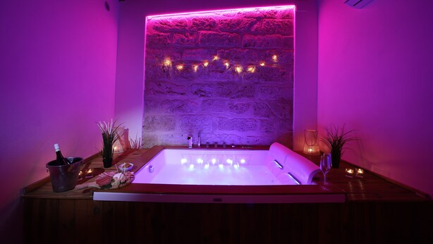 Um quarto de spa com parede de pedra, uma banheira, velas e uma garrafa de vinho.
