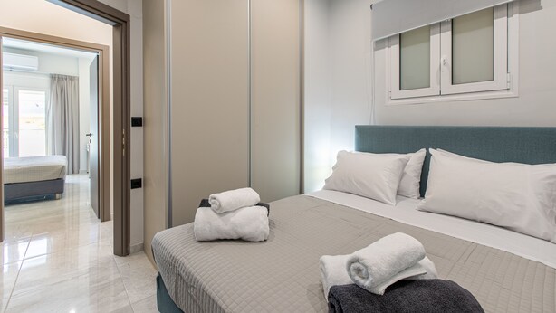 Quarto de hotel moderno com uma cama grande, área de estar separada e vista para o corredor.