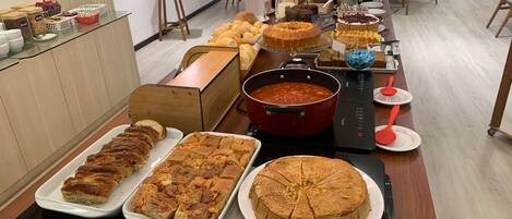 Disposição de buffet com diversos pratos, uma panela vermelha em um fogão por indução e uma área de refeições com cadeiras e mesas.
