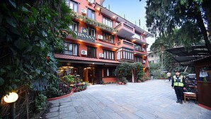 Um hotel com fachada vermelha, várias varandas e uma área de jardim bem cuidada.