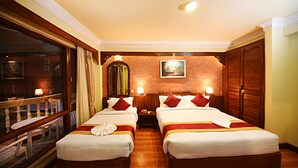 Quarto de hotel com duas camas, piso de madeira, uma janela grande com cortinas, um quadro na parede e um guarda-roupa de madeira.
