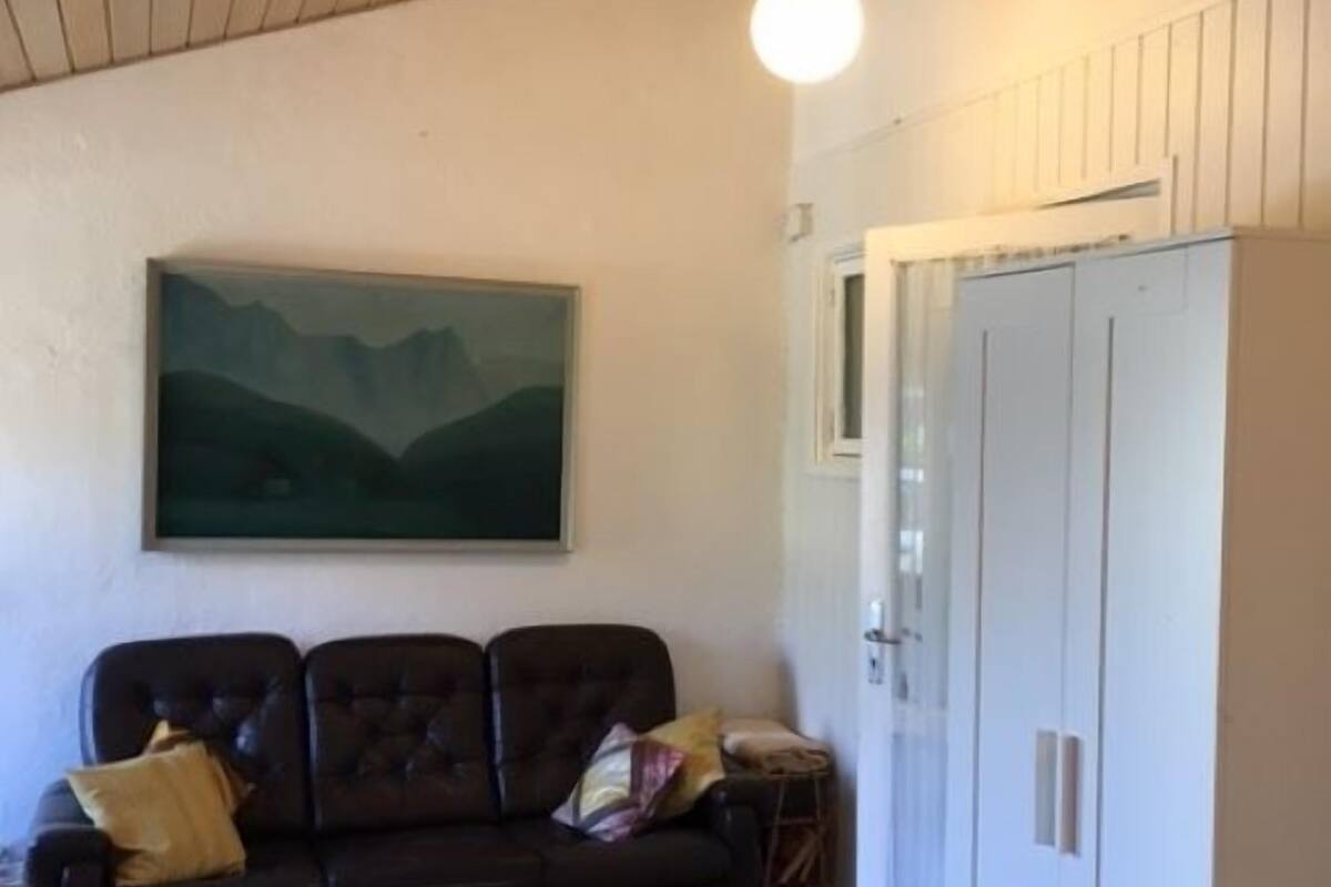Quarto com teto de madeira, sofá marrom escuro com almofadas, guarda-roupa branco e uma pintura de montanhas na parede.