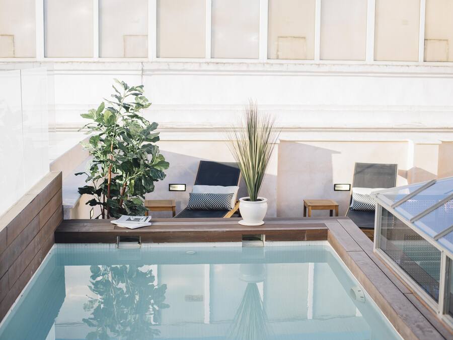 Área de piscina no terraço, com espaço para sentar, plantas em vasos e estrutura de vidro.