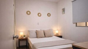 Quarto com cama, duas mesas de cabeceira, luminárias fixadas na parede e três objetos decorativos na parede.