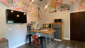 Cozinha moderna com televisão de tela plana, banquetas de madeira, mesa de jantar e um mural colorido na parede.