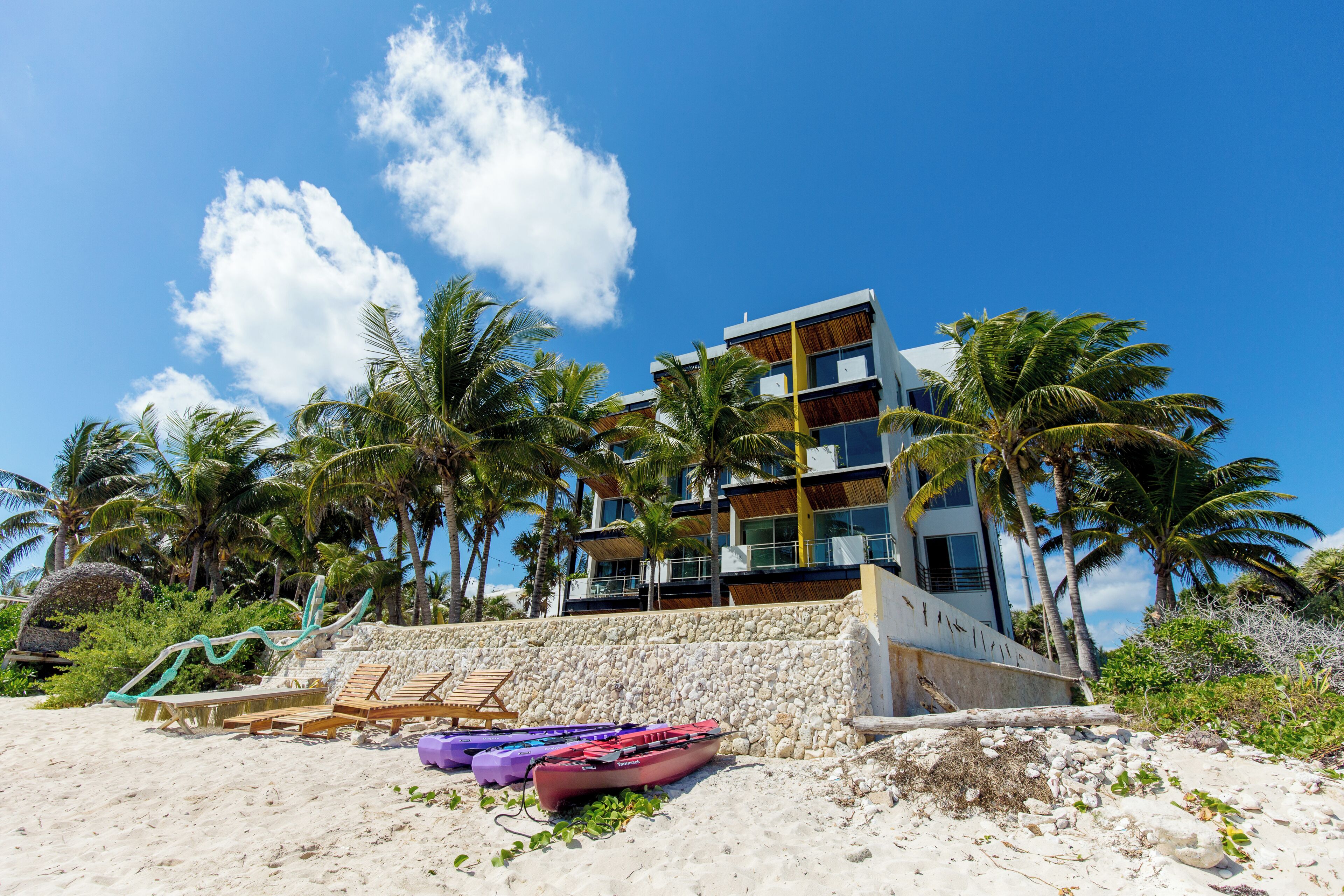 Um hotel à beira-mar com uma parede de pedra, palmeiras e um céu azul límpido.