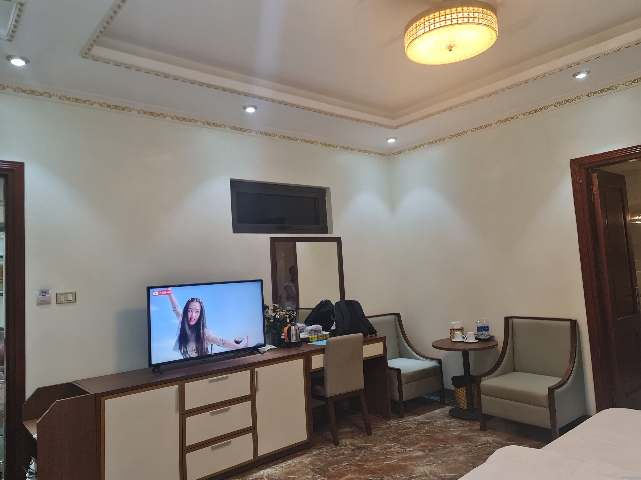 Quarto de hotel com televisão, escrivaninha, cadeira, cama e pequena mesa com luminária.