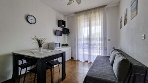 Um espaço compacto com mesa de jantar, duas cadeiras, sofá, televisão e relógio na parede.