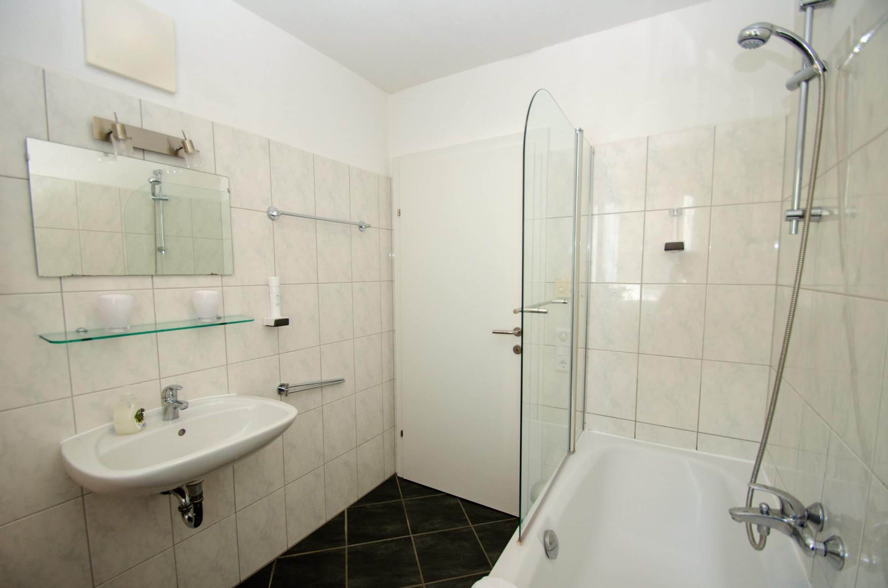 Casa de banho com cabine de duche em vidro, lavatório branco com espelho em cima e prateleira de vidro.