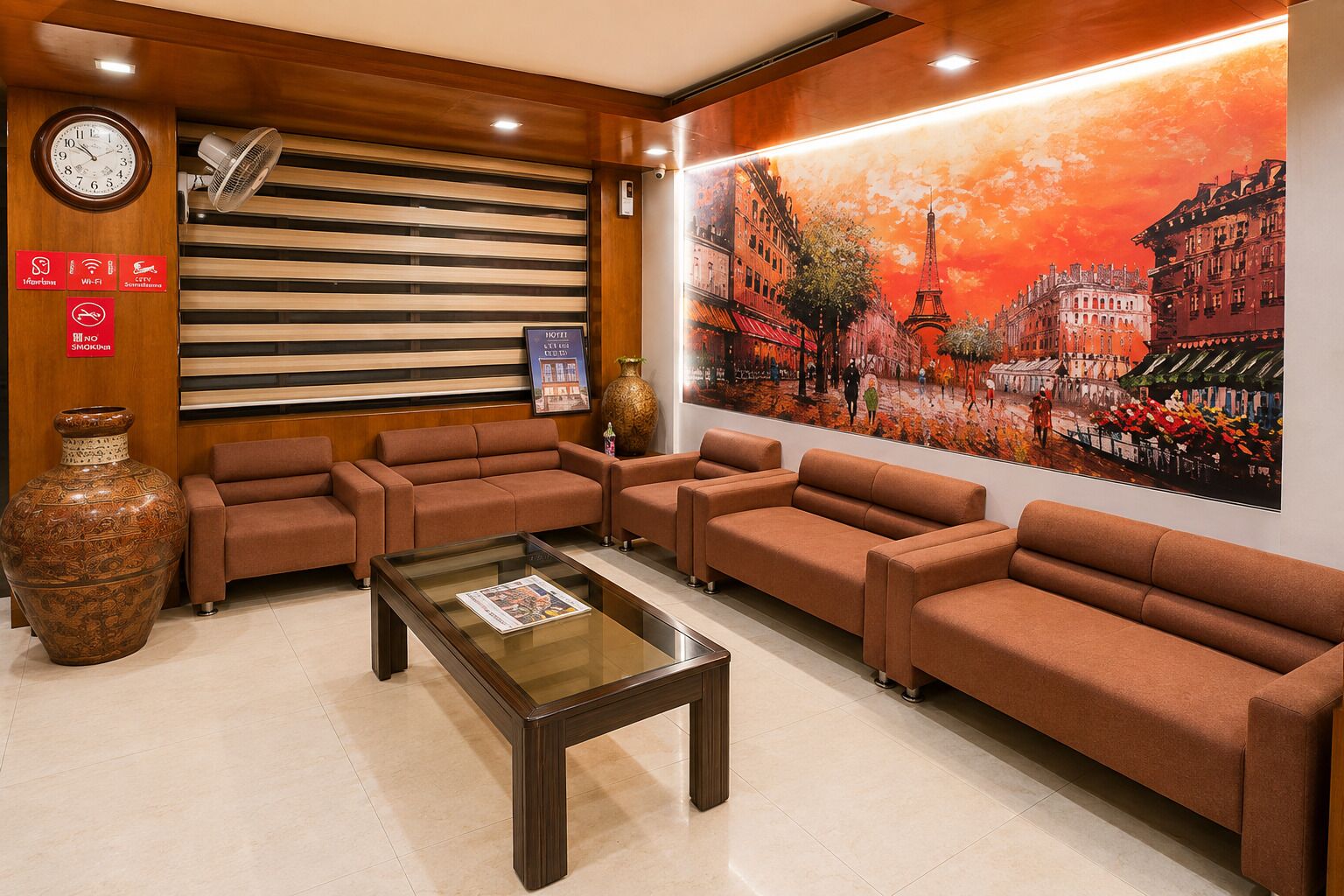 Um hall de hotel com uma grande pintura de uma paisagem urbana, um relógio e um ventilador.