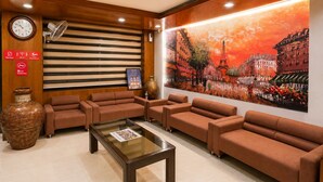 Um hall de hotel com uma grande pintura de uma paisagem urbana, um relógio e um ventilador.