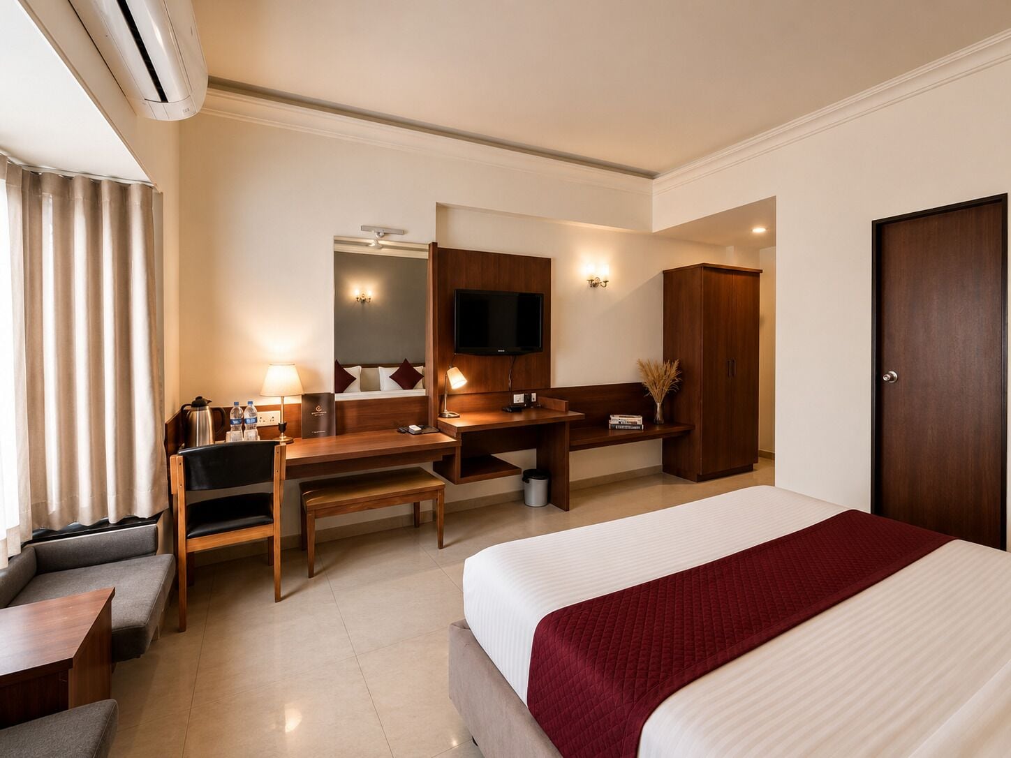Quarto de hotel com cama, escrivaninha, cadeira e televisão.