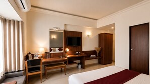 Quarto de hotel com cama, escrivaninha, cadeira e televisão.