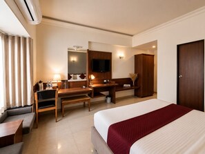 Quarto de hotel com cama, escrivaninha, cadeira e televisão.