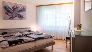 Quarto moderno com cama, mesa de cabeceira, abajur e uma grande pintura abstrata na parede.
