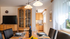 Uma sala de jantar com uma mesa de madeira posta para seis pessoas, uma televisão e um armário com portas de vidro.