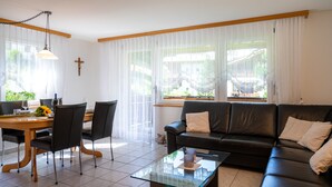 Uma sala de estar com mesa de jantar, sofá de couro preto e mesa de centro de vidro.