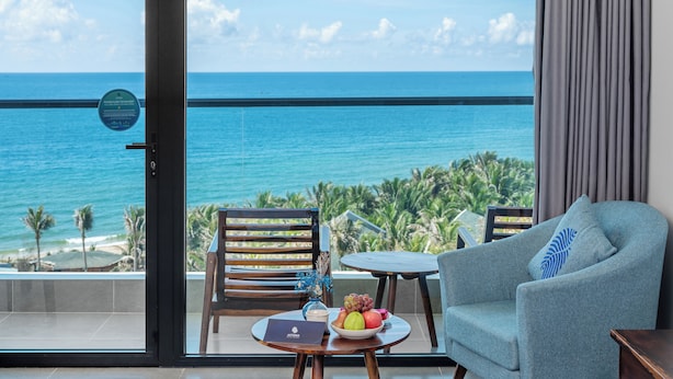 Varanda com vista para o oceano, uma cadeira, uma mesa com uma fruteira e uma placa na porta.
