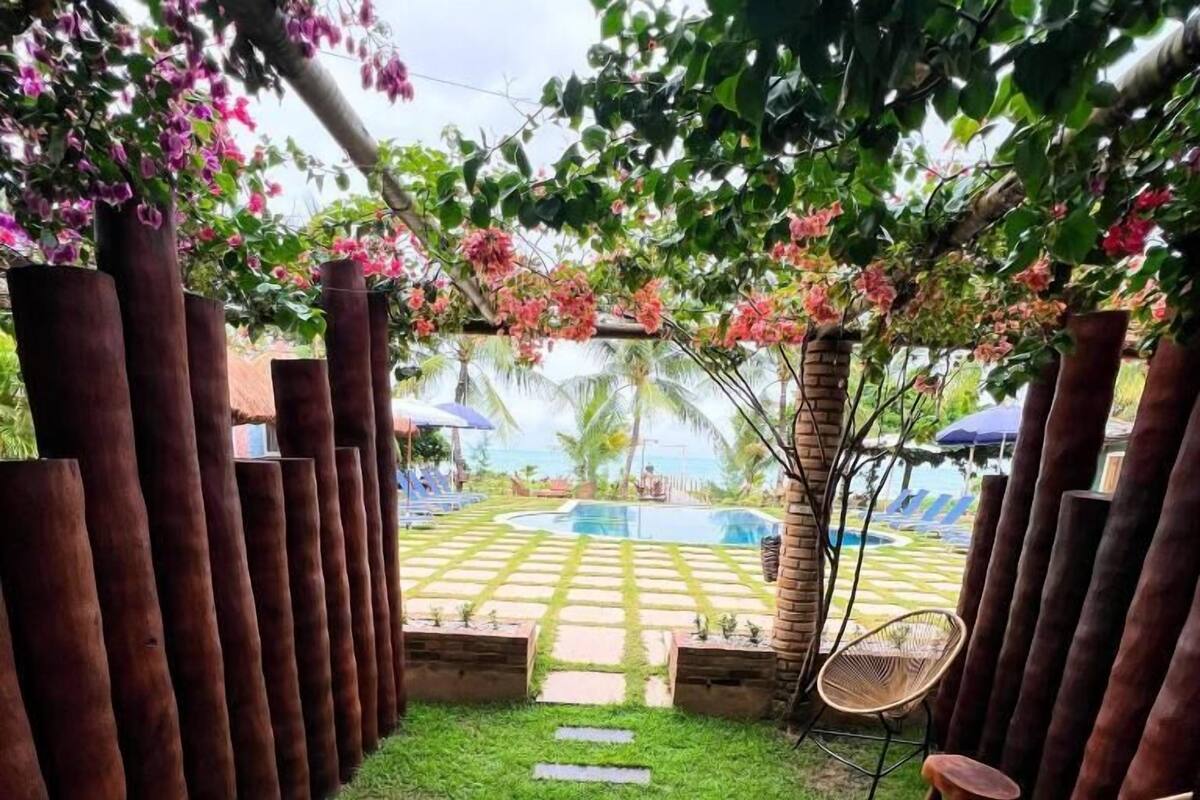 Um deck de madeira com área gramada, piscina e espreguiçadeiras.