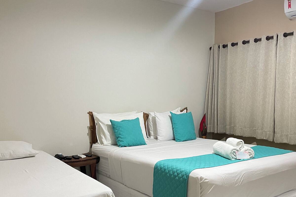 Quarto de hotel com duas camas de solteiro, uma mesa de cabeceira e uma luminária no teto.