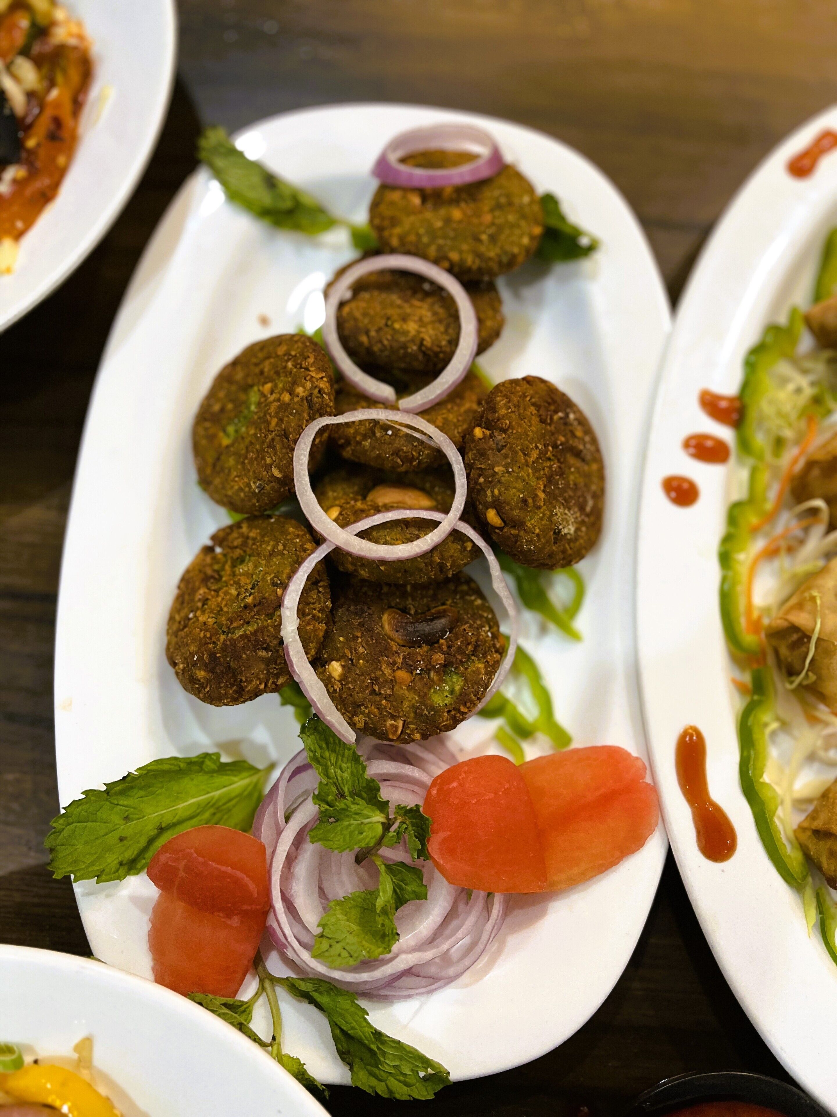 Um prato de falafel com guarnições de cebola roxa, salsa e fatias de tomate.