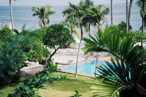 Uma área de piscina com palmeiras, espreguiçadeiras e vista para o oceano.