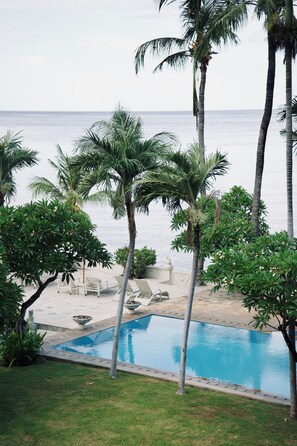 Área da piscina com vista para o oceano, cercada por palmeiras e espreguiçadeiras.