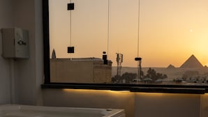 Casa de banho com banheira, um banco de madeira e vista para uma pirâmide e o horizonte urbano ao pôr do sol.