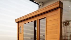 Uma sauna de madeira com porta de vidro e uma pequena placa na parede.