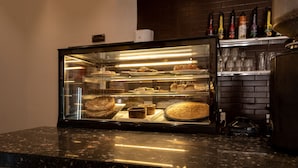 Vitrine de padaria com diversos produtos de pastelaria e uma seleção de acompanhamentos no balcão.