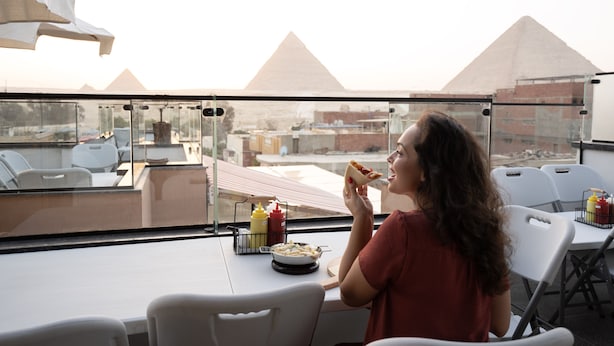 Uma pessoa jantando à mesa com vista para as pirâmides.