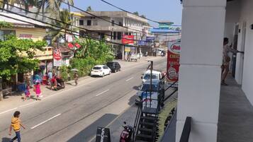 Vista da rua com uma scooter vermelha estacionada na calçada, uma faixa de pedestres e diversos estabelecimentos comerciais e edifícios ao fundo.
