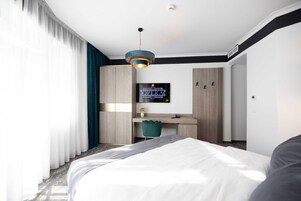 Quarto de hotel moderno com cama, escrivaninha, televisão e guarda-roupa.