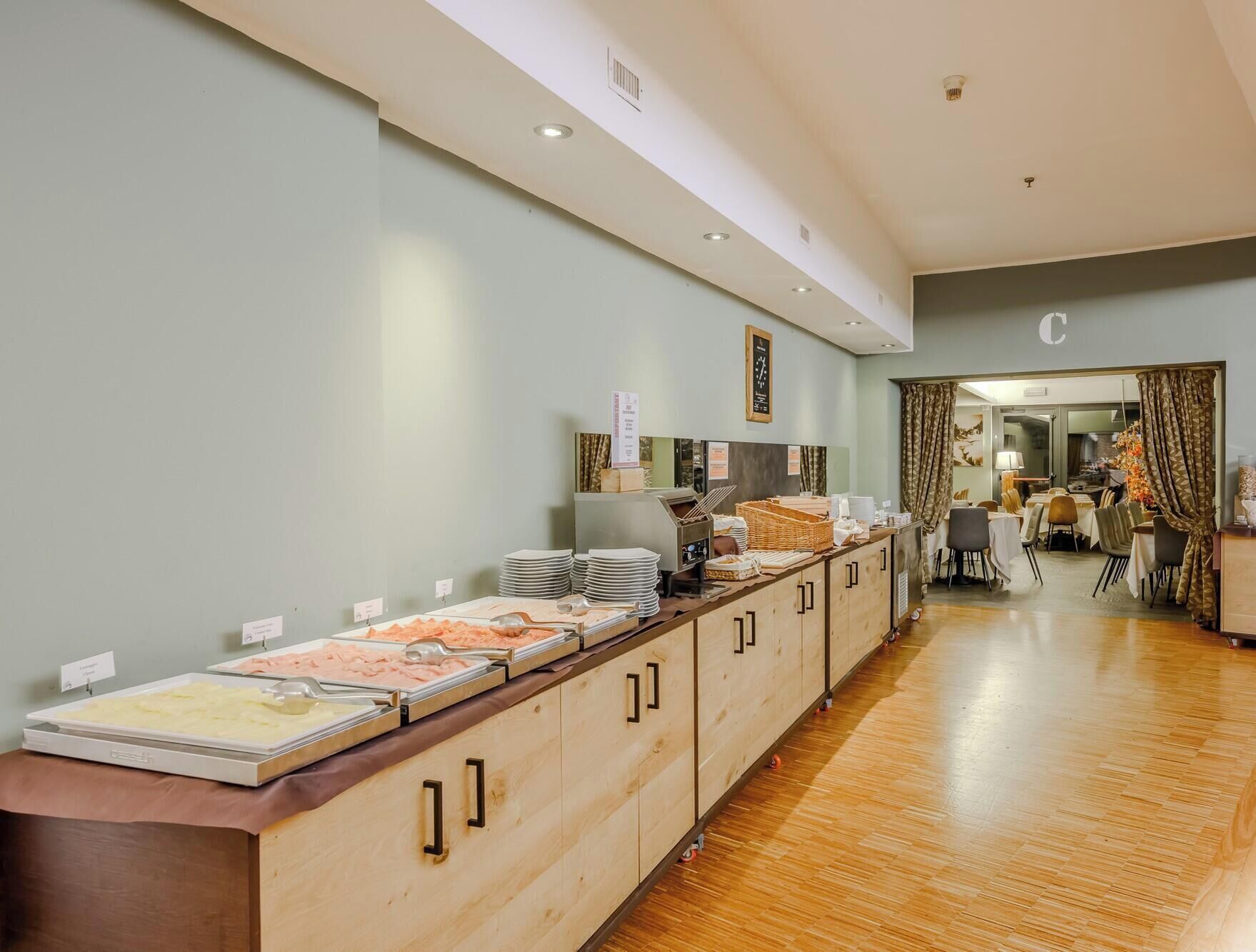 Uma área de buffet com várias estações de comida, um relógio e um espaço de refeições com mesas e cadeiras.