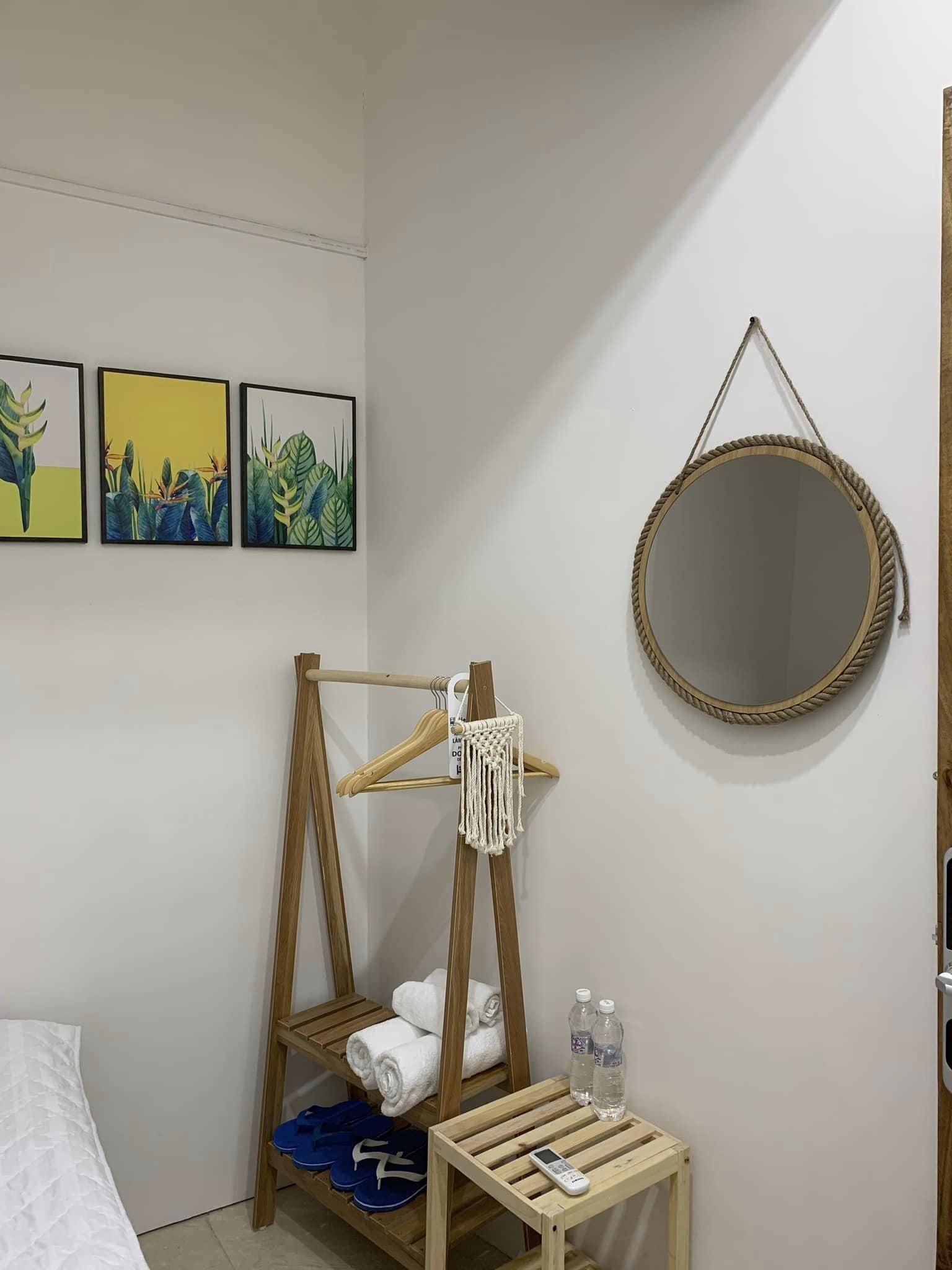 Quarto com estrutura de cama de madeira, um macramê pendurado, um espelho redondo e obras de arte na parede.