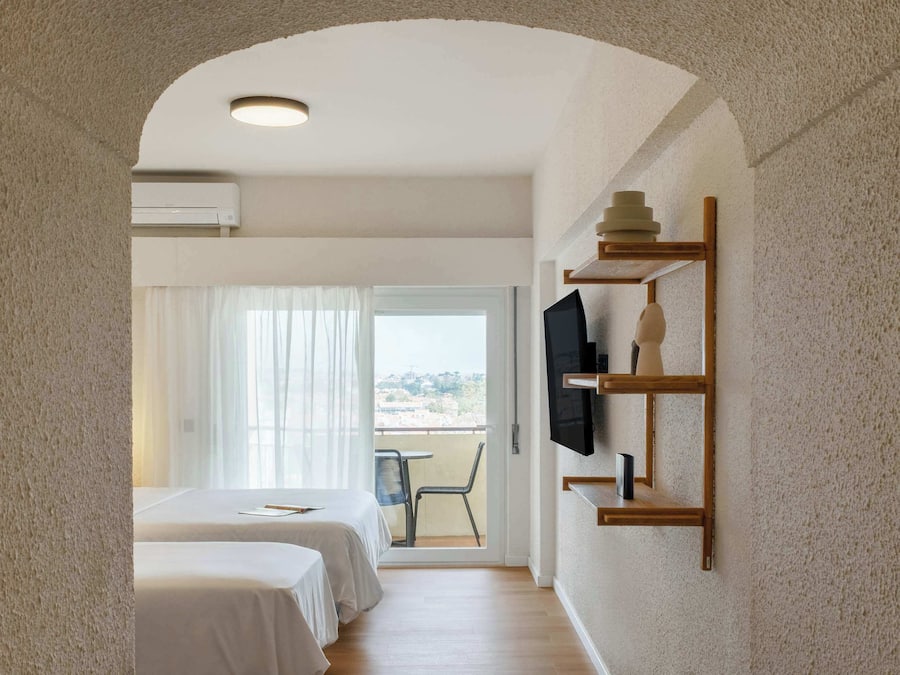 Quarto de hotel com duas camas, televisão na parede e varanda com vista.